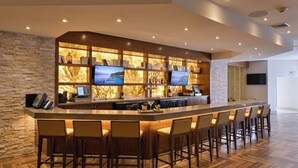 Uma área de bar moderna com um balcão comprido, várias TVs e banquetas.