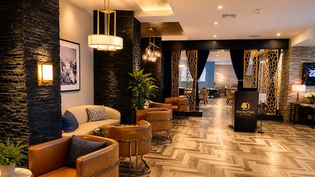 Um saguão de hotel com assentos de couro, uma recepção e um piso de madeira em padrão herringbone.