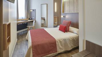 Quarto de hotel com cama, escrivaninha, cadeira, televisão e espelho.
