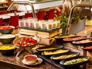 Buffet com diversos alimentos, incluindo frutas, queijos e carnes.