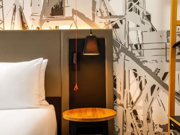 Quarto de hotel com uma cama, uma pequena mesa redonda de madeira, uma luminária de parede e parede com padrão.