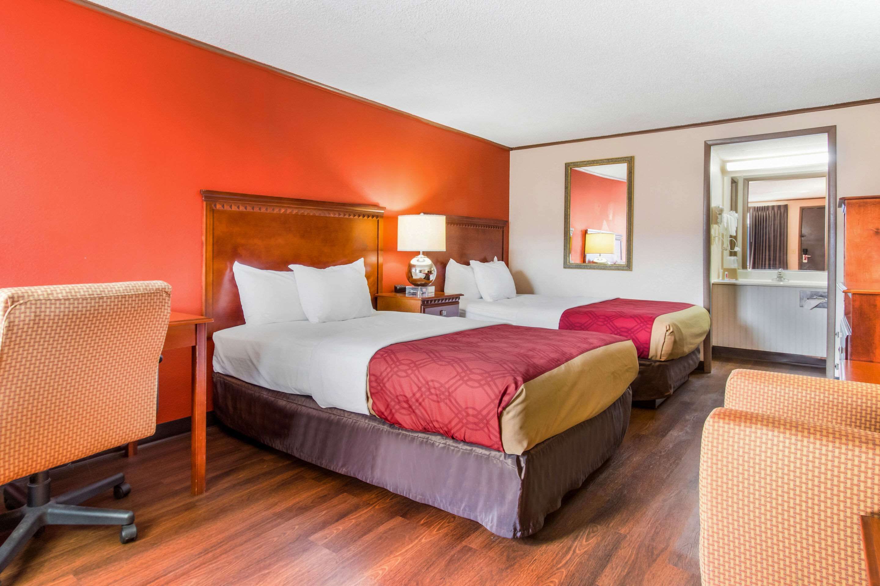 Quarto de hotel com duas camas, uma escrivaninha, uma cadeira e um espelho.