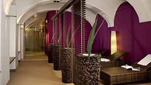 Uma área de spa com um longo corredor, teto abobadado e um espaço de estar com sofá de fibra natural e uma mesinha.