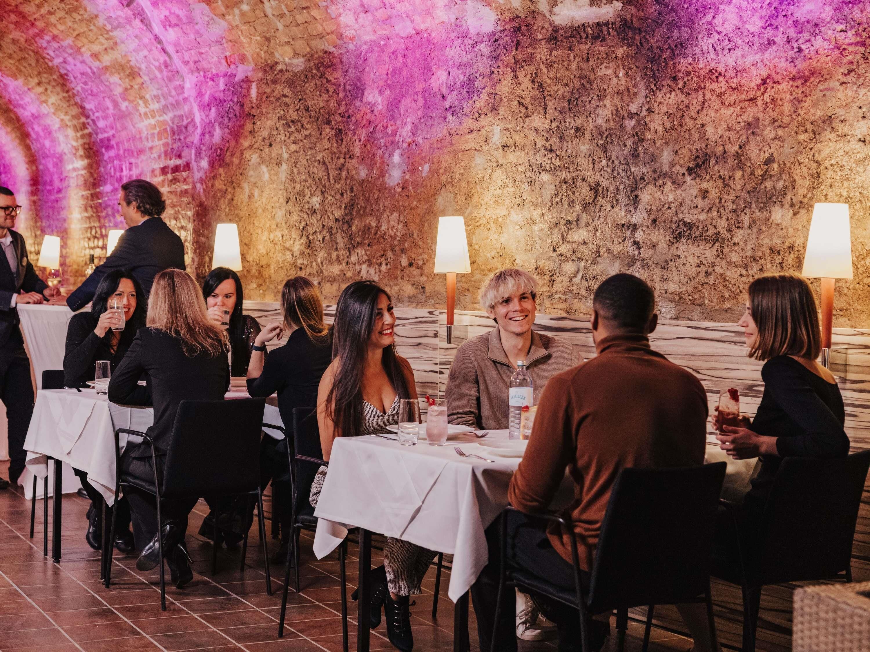Restaurante com mesas postas para refeição, parede de pedra ao fundo e um candelabro.