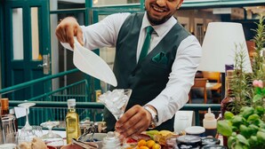 Uma pessoa servindo bebidas em uma mesa com diversos frascos, copos e acompanhamentos.