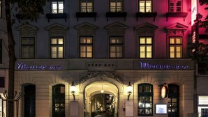 Exterior do Hotel Mercure com fachada clássica, entrada em arco e janelas iluminadas.