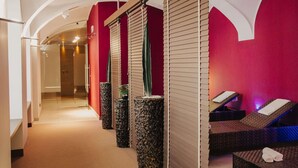 Um espaço de spa com cadeira de massagem, uma mesinha com toalhas e uma parede com detalhes em vermelho.