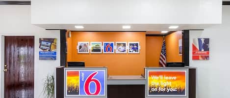 Uma receção com um grande sinal numérico '6', um vaso de planta e uma parede com fotografias emolduradas e uma bandeira americana.