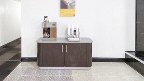 Uma área de recepção com máquina de café, bebedouro e um quadro na parede.
