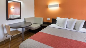 Quarto de hotel com cama, escrivaninha, cadeira e espelho.