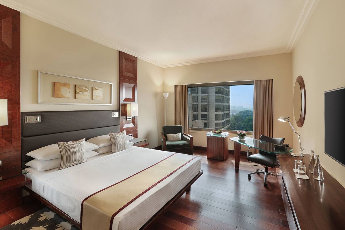 Quarto de hotel com uma cama grande, uma escrivaninha, uma cadeira, uma televisão e uma janela com vista para a cidade.