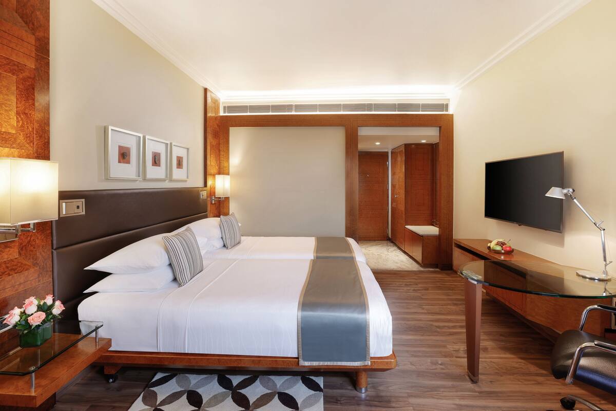 Quarto de hotel com uma cama grande, mesas de cabeceira, uma escrivaninha, televisão e quadros na parede.