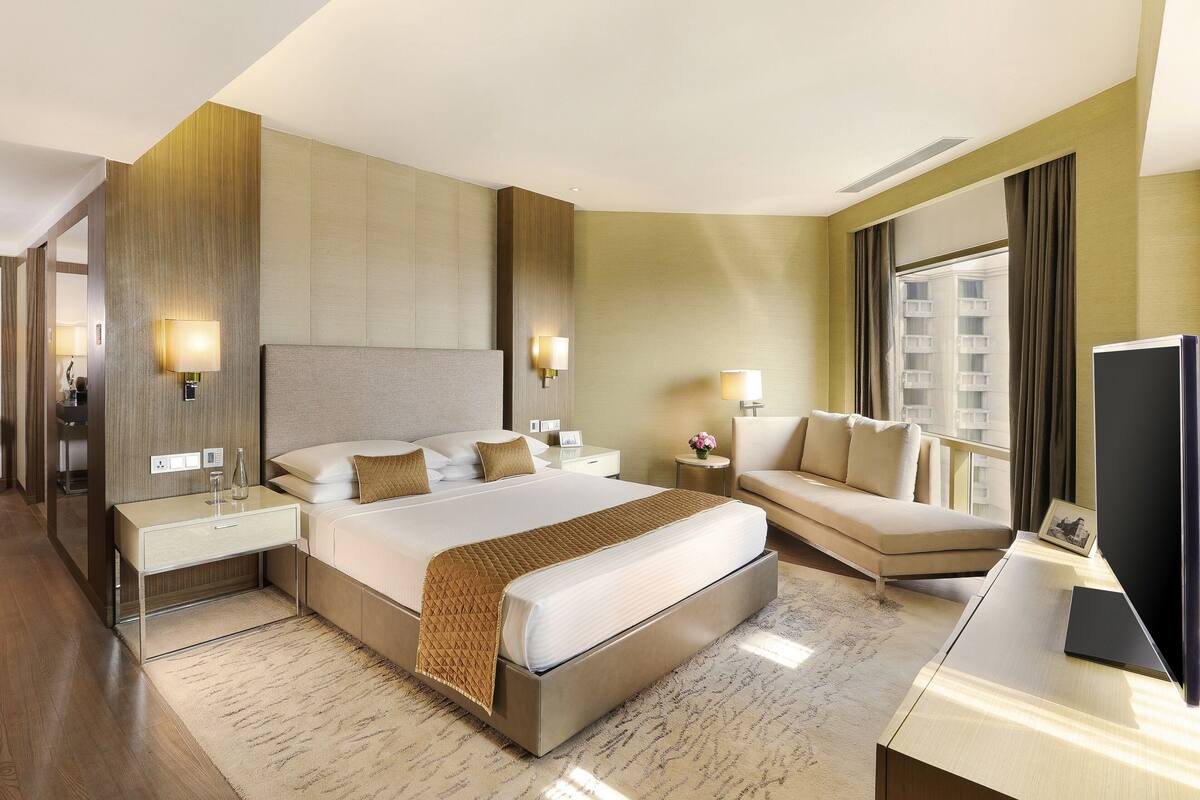 Quarto de hotel moderno com uma cama grande, mesas de cabeceira, escrivaninha, televisão e janela com cortinas.