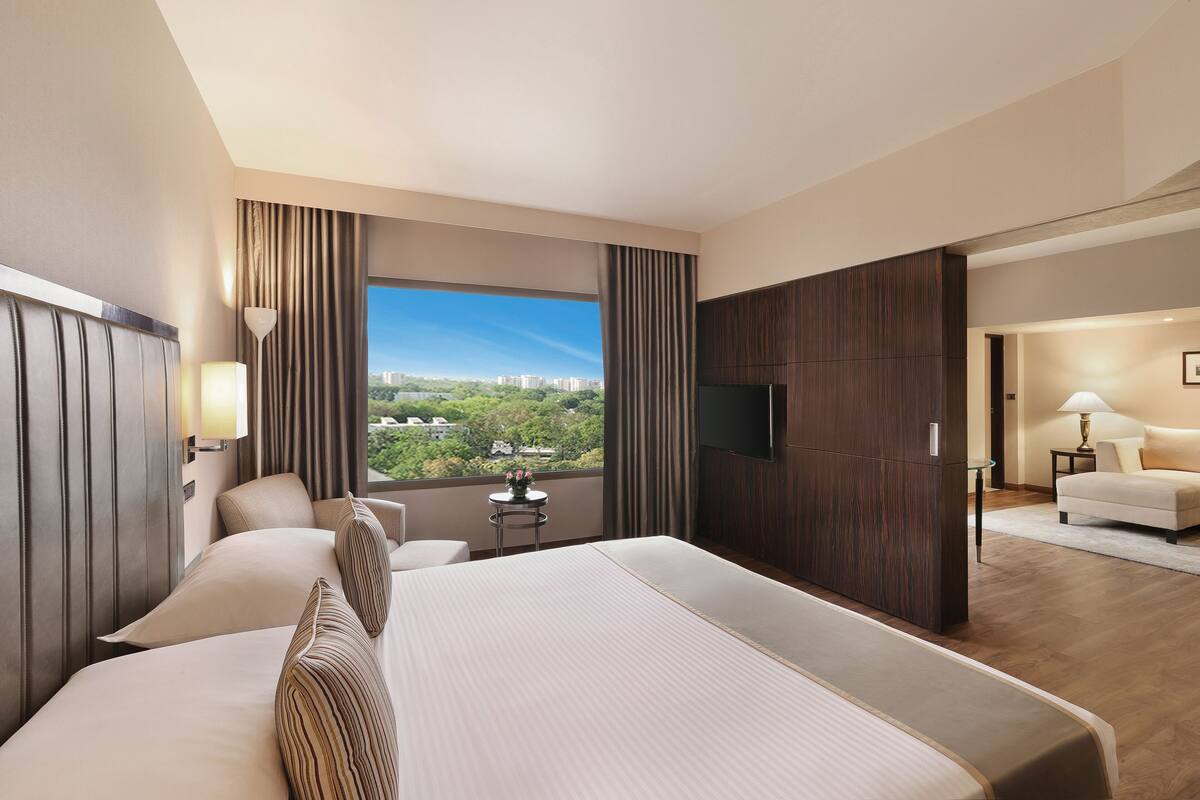 Quarto de hotel com uma cama grande, televisão, escrivaninha e vista para a paisagem urbana.