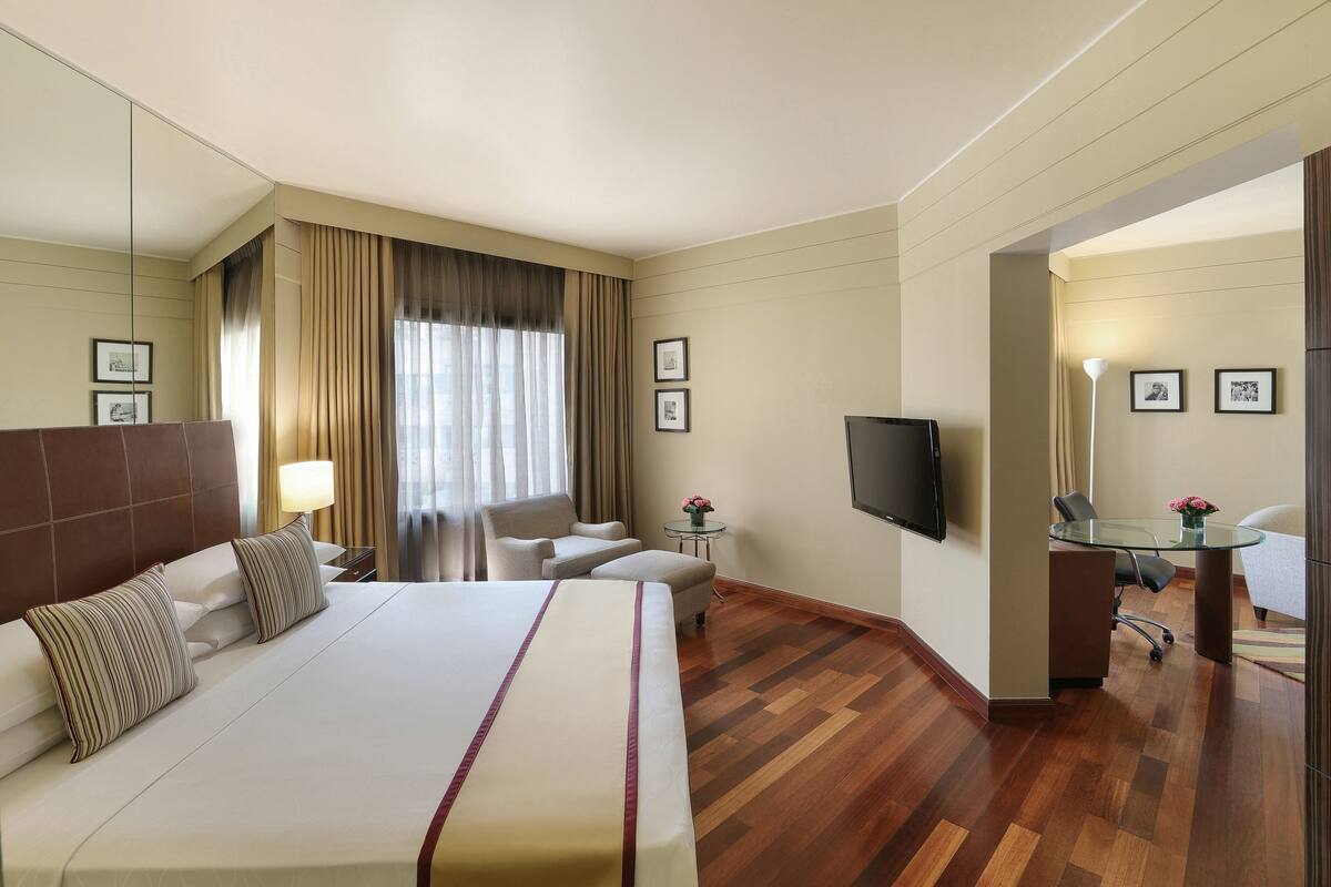 Quarto de hotel com uma cama grande, uma escrivaninha, uma cadeira e uma televisão.