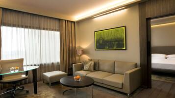 Quarto de hotel com sofá, mesa de centro redonda, uma cadeira, cama e um quadro na parede.