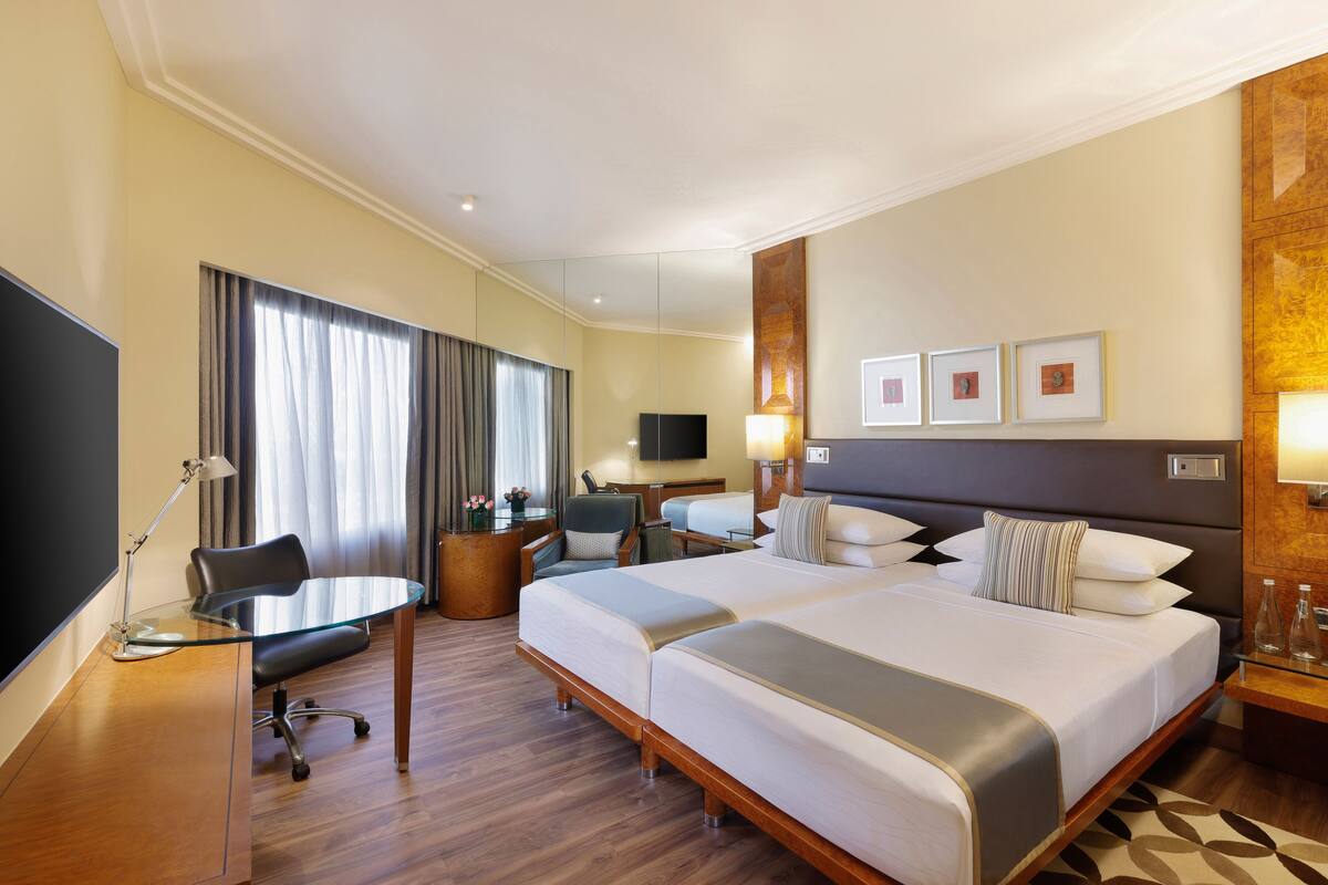 Quarto de hotel com uma cama grande, uma escrivaninha com cadeira, televisão e uma janela com cortinas.