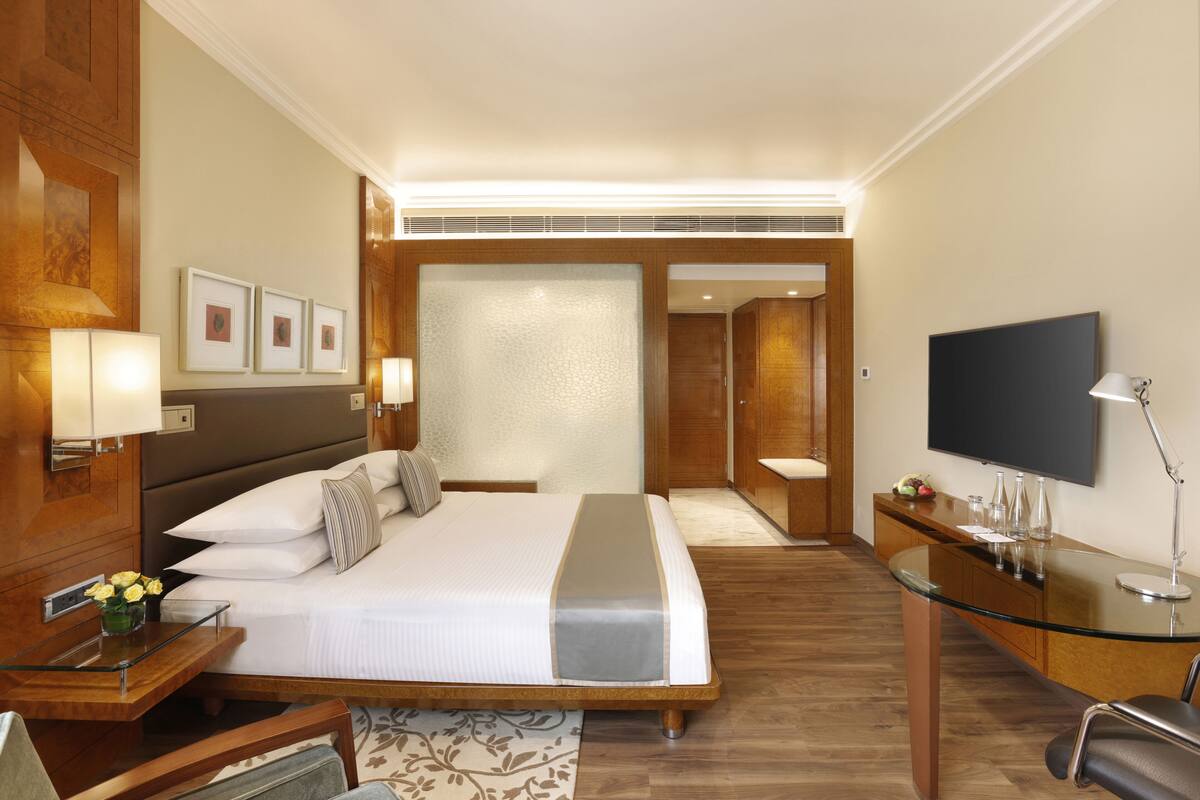 Quarto de hotel com uma cama grande, mesas de cabeceira, uma escrivaninha com cadeira, televisão de tela plana e quadros nas paredes.