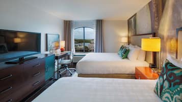 Quarto de hotel com duas camas, uma escrivaninha, uma televisão e vista para o exterior.