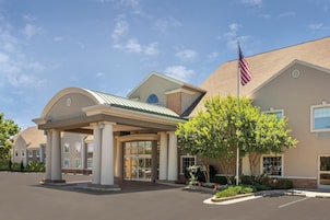 Entrada de hotel com galeria coberta, uma bandeira e área ajardinada com árvores.
