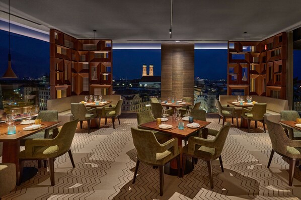 Restaurante com vista para a cidade, com mesas e cadeiras dispostas para refeições.