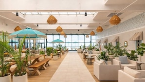 Um espaço interno amplo com mesas de madeira, plantas em vasos e mobiliário moderno.