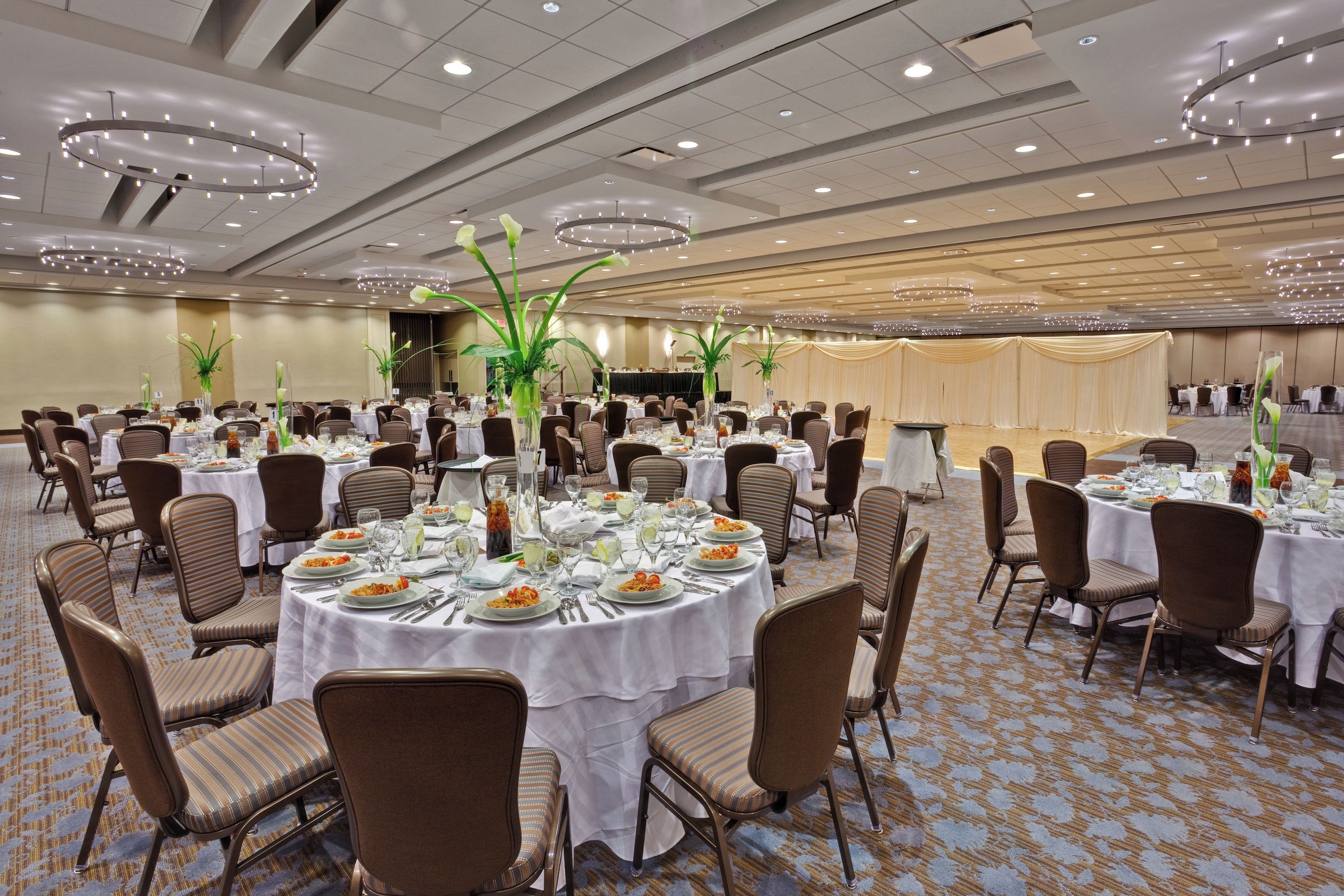 Salão de banquetes com mesas redondas, cadeiras e centros de mesa com flores.