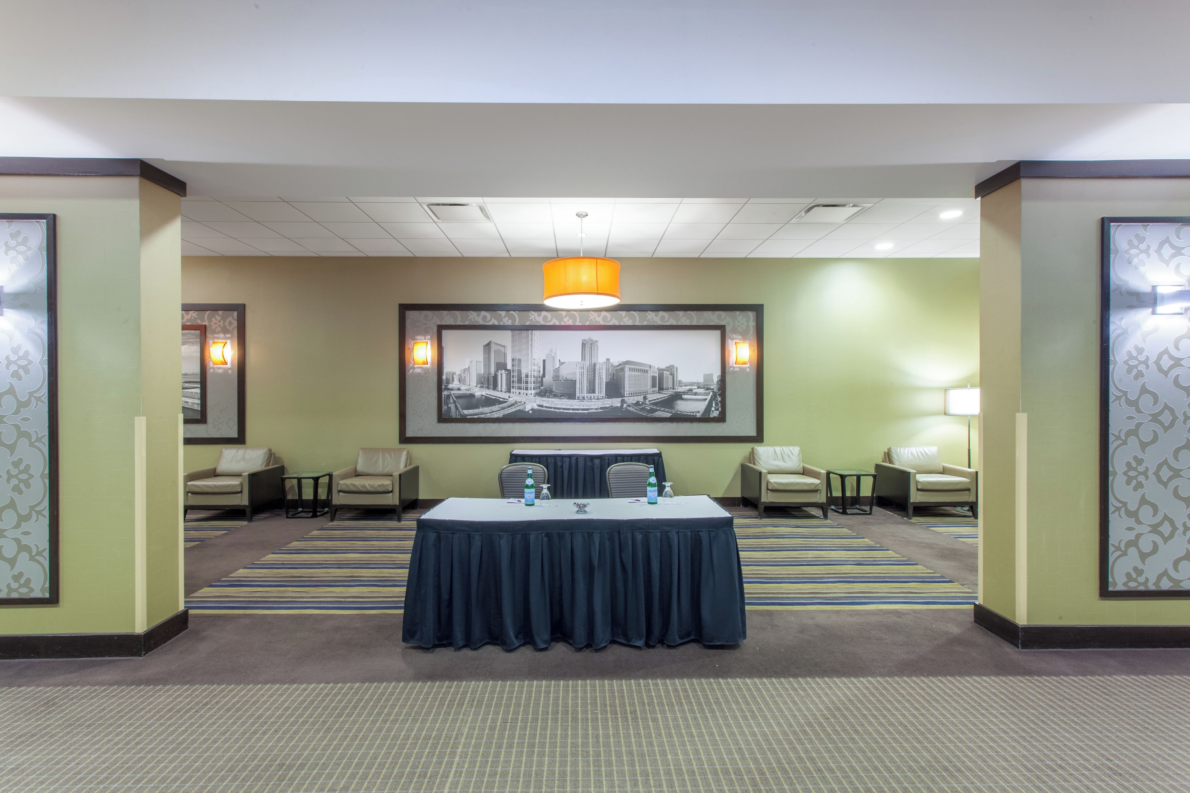 Sala de conferência com mesa, cadeiras, pintura de paisagem urbana e paredes com padrão.
