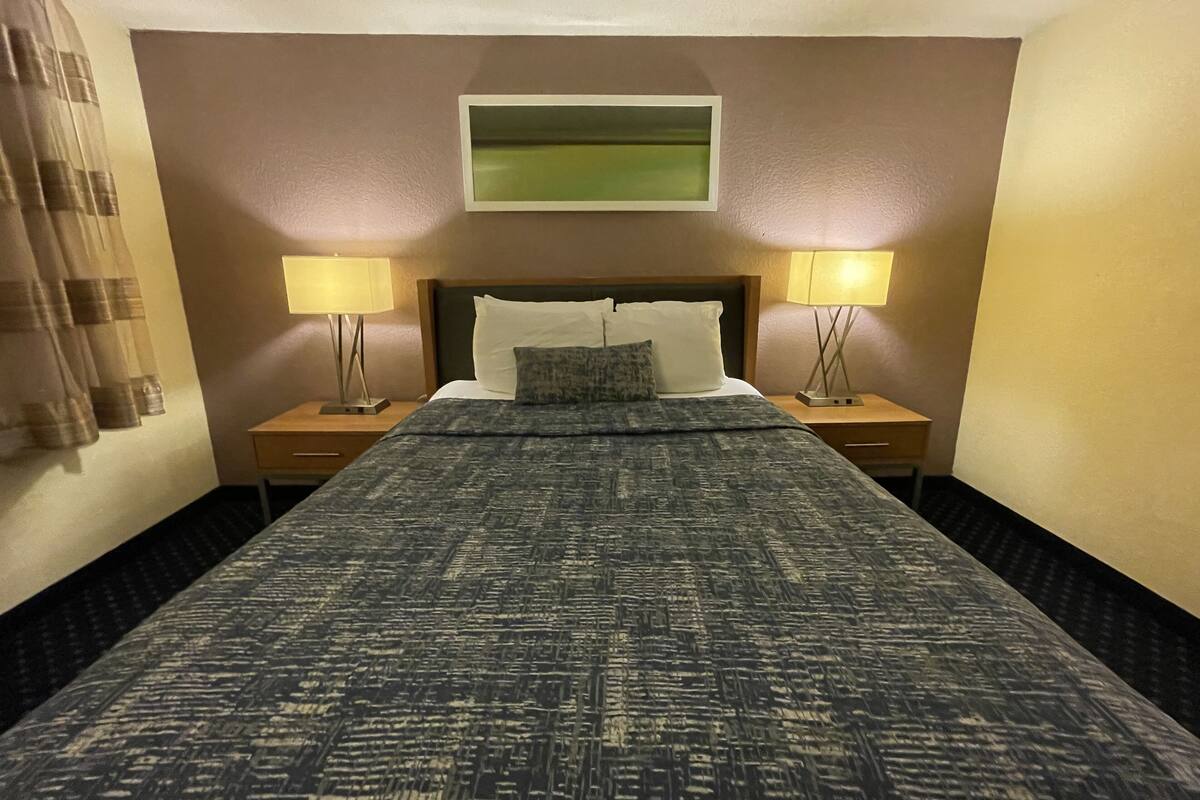 Quarto de hotel com uma cama grande, duas mesas de cabeceira com abajures, uma cabeceira e um quadro pendurado na parede.