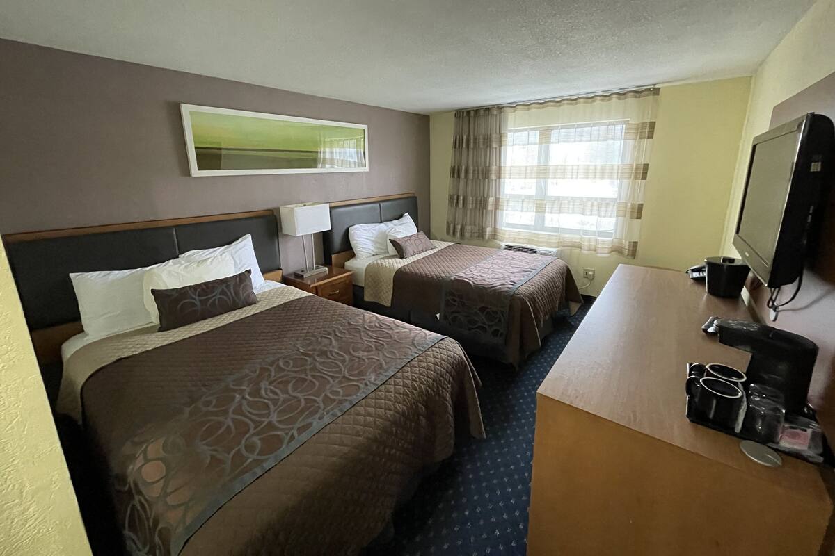 Quarto de hotel com duas camas, uma escrivaninha, televisão e janela com cortinas.