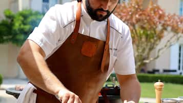 Um chef preparando comida ao ar livre, com uma churrasqueira e diversos utensílios de cozinha.