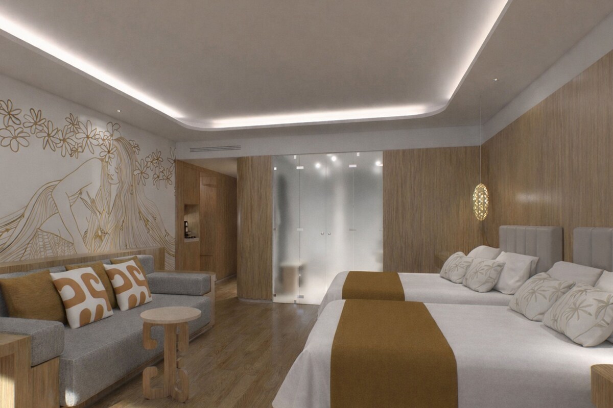 Quarto de hotel moderno com sofá, cama, mesa redonda e um mural decorativo na parede.