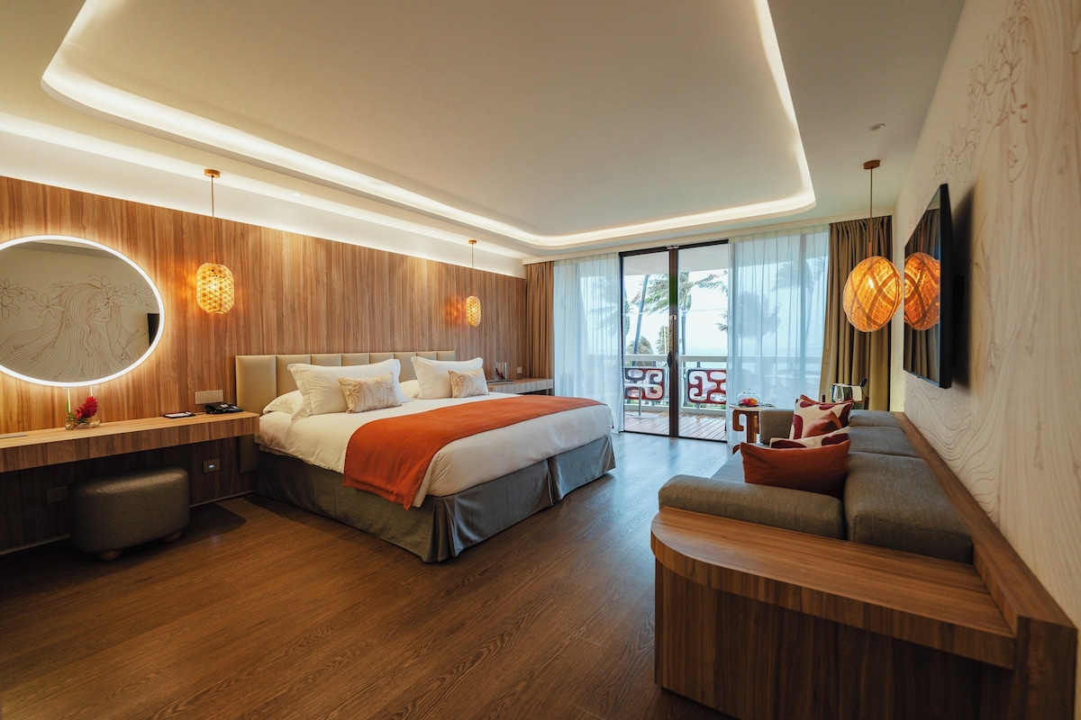 Quarto de hotel moderno com cama grande, área de estar e varanda com vista.