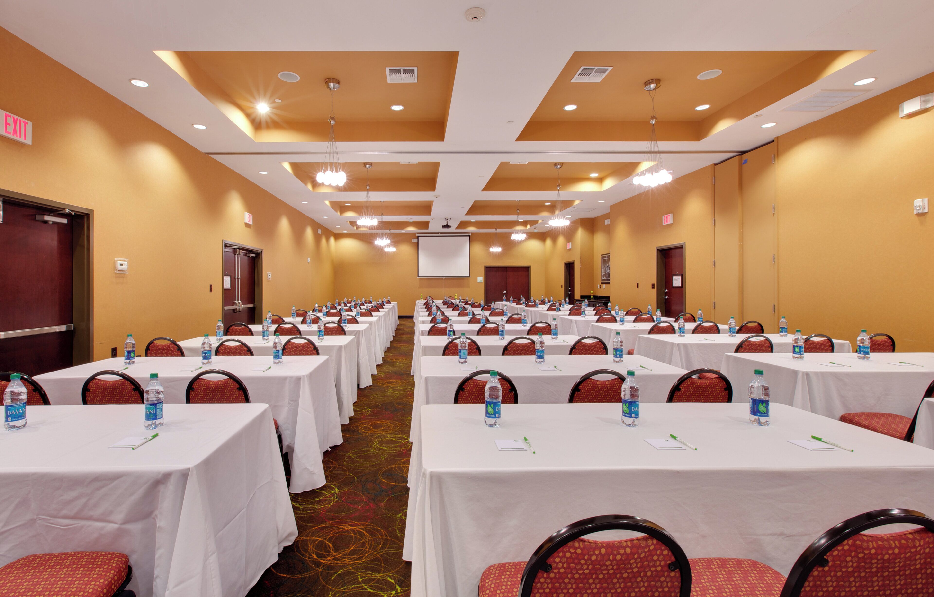 Sala de conferências com várias mesas, cadeiras e garrafas de água.