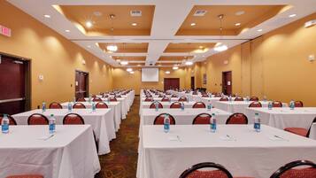 Sala de conferências com várias mesas, cadeiras e garrafas de água.