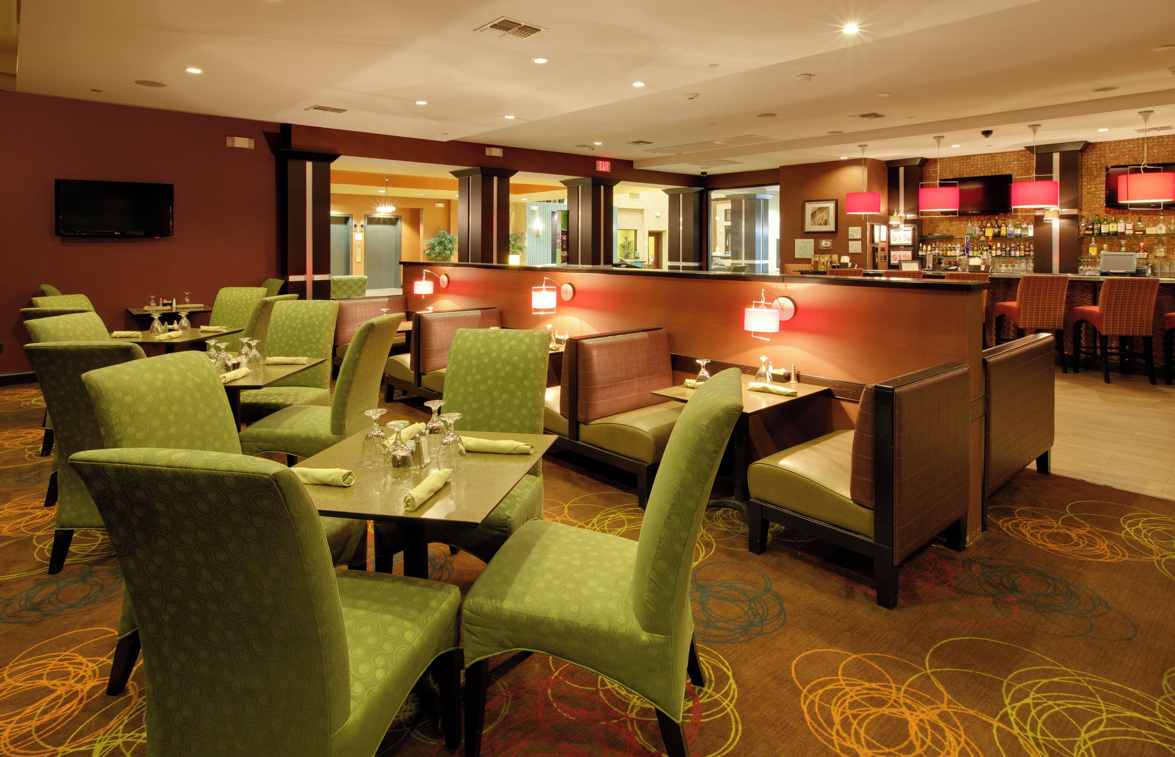 Uma sala de jantar de hotel com cabines e mesas, um bar e uma televisão na parede.