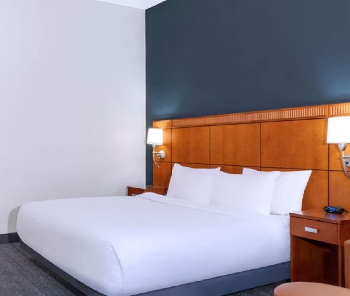 Quarto de hotel com uma cama grande, cabeceira de madeira, duas mesas de cabeceira com luminárias e uma parede escura de destaque.