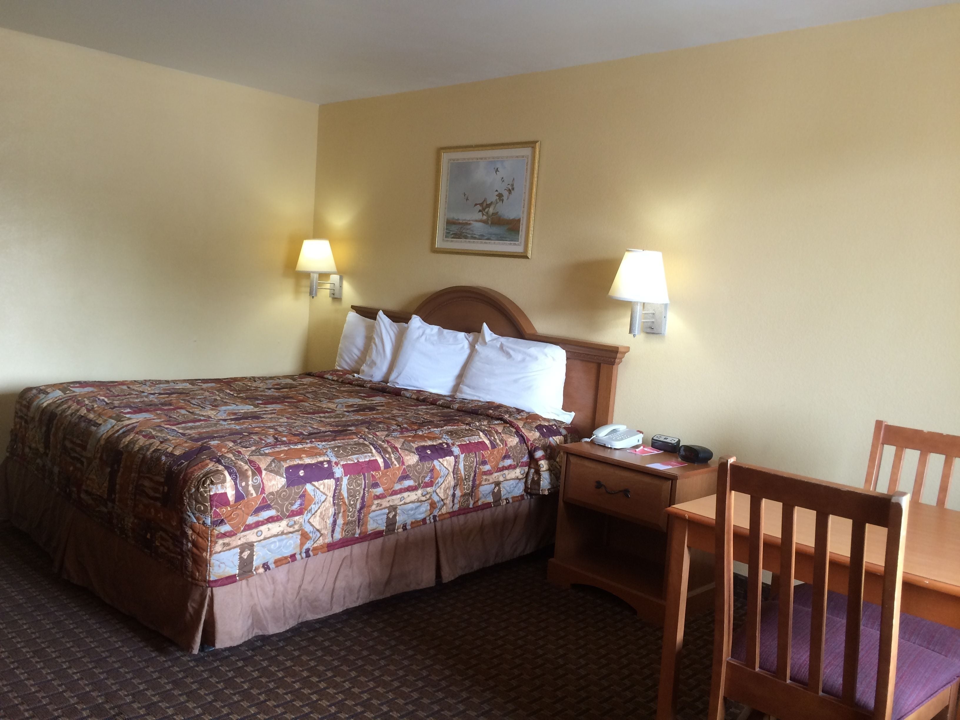 Quarto de hotel com uma cama grande, duas luminárias de cabeceira, uma mesa de cabeceira de madeira, um telefone e uma cadeira.
