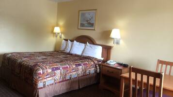 Quarto de hotel com uma cama grande, duas luminárias de cabeceira, uma mesa de cabeceira de madeira, um telefone e uma cadeira.
