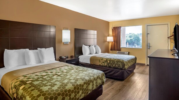 Quarto de hotel com duas camas, uma escrivaninha, televisão e janela com cortinas.