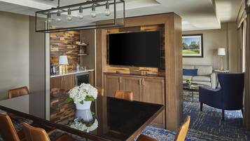 Quarto de hotel moderno com área de refeições, cozinha, TV de tela plana e canto de estar com uma poltrona azul.