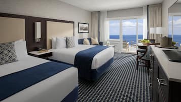 Quarto de hotel com duas camas, uma escrivaninha com luminária, uma cadeira e vista para o oceano.