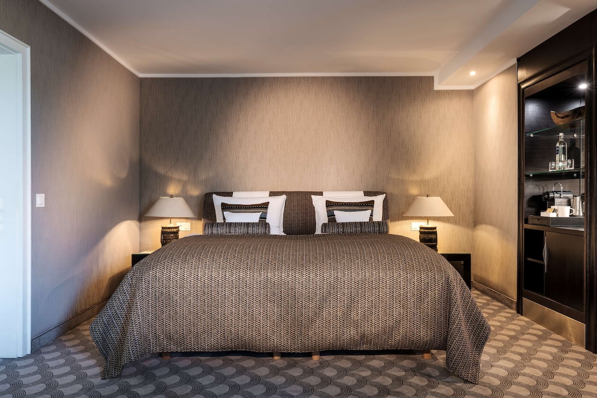 Quarto bem arrumado com cama grande, duas mesas de cabeceira com abajures, armário embutido e pequena cozinha.