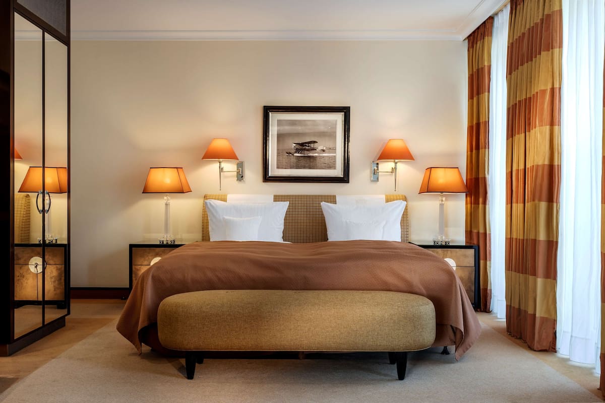 Quarto de hotel com uma cama grande, duas mesas de cabeceira com luminárias, um quadro na parede e um espelho.