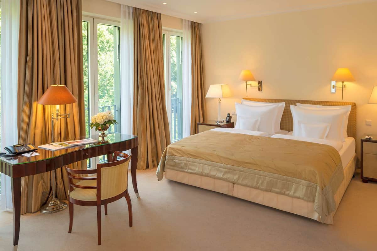 Quarto de hotel com uma cama, duas luminárias de cabeceira, uma escrivaninha com telefone e uma cadeira.