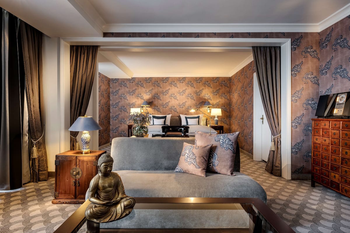 Quarto com sofá, estátua de Buda, armário de madeira e cama com papel de parede estampado.
