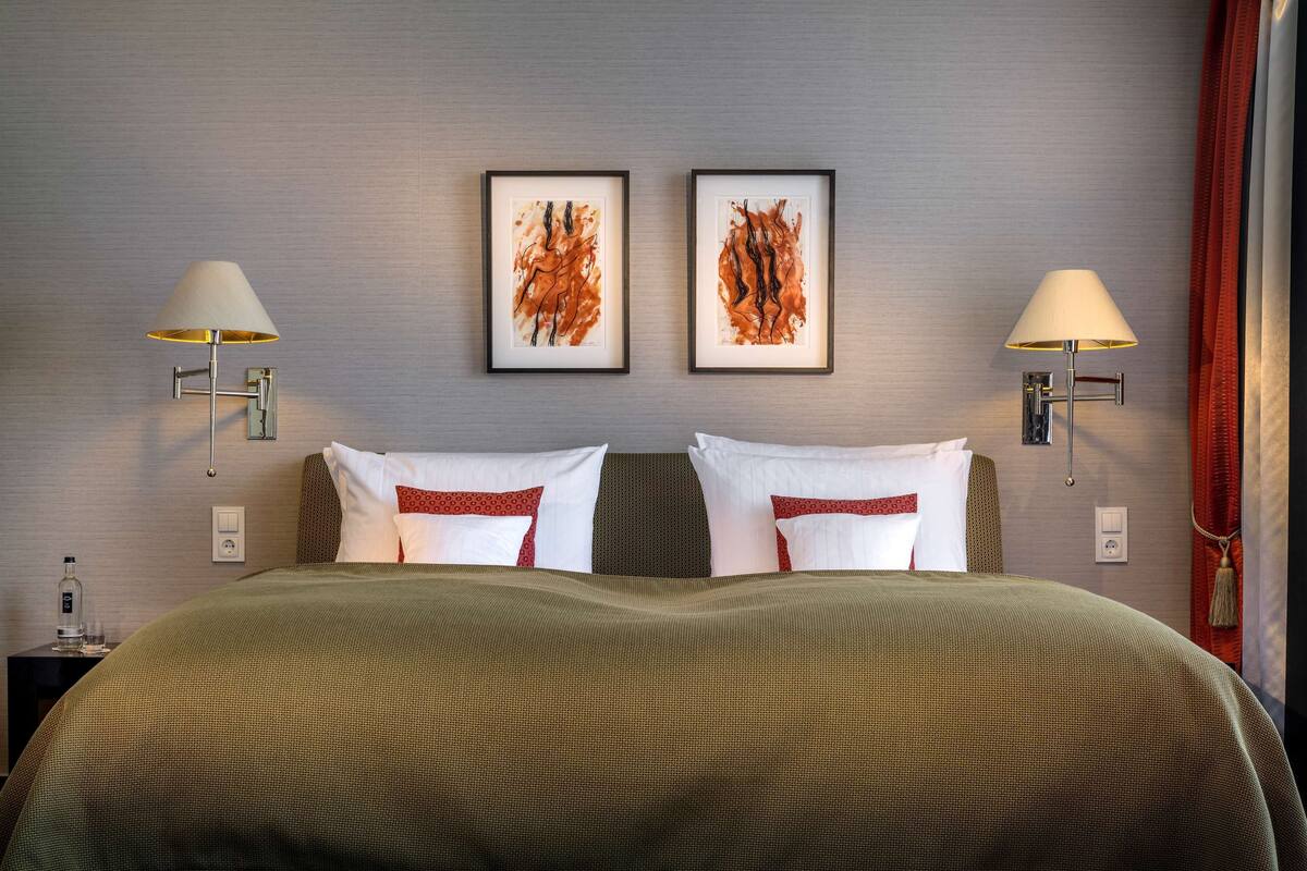 Quarto de hotel com uma cama grande, duas luminárias fixadas na parede e duas obras de arte emolduradas.