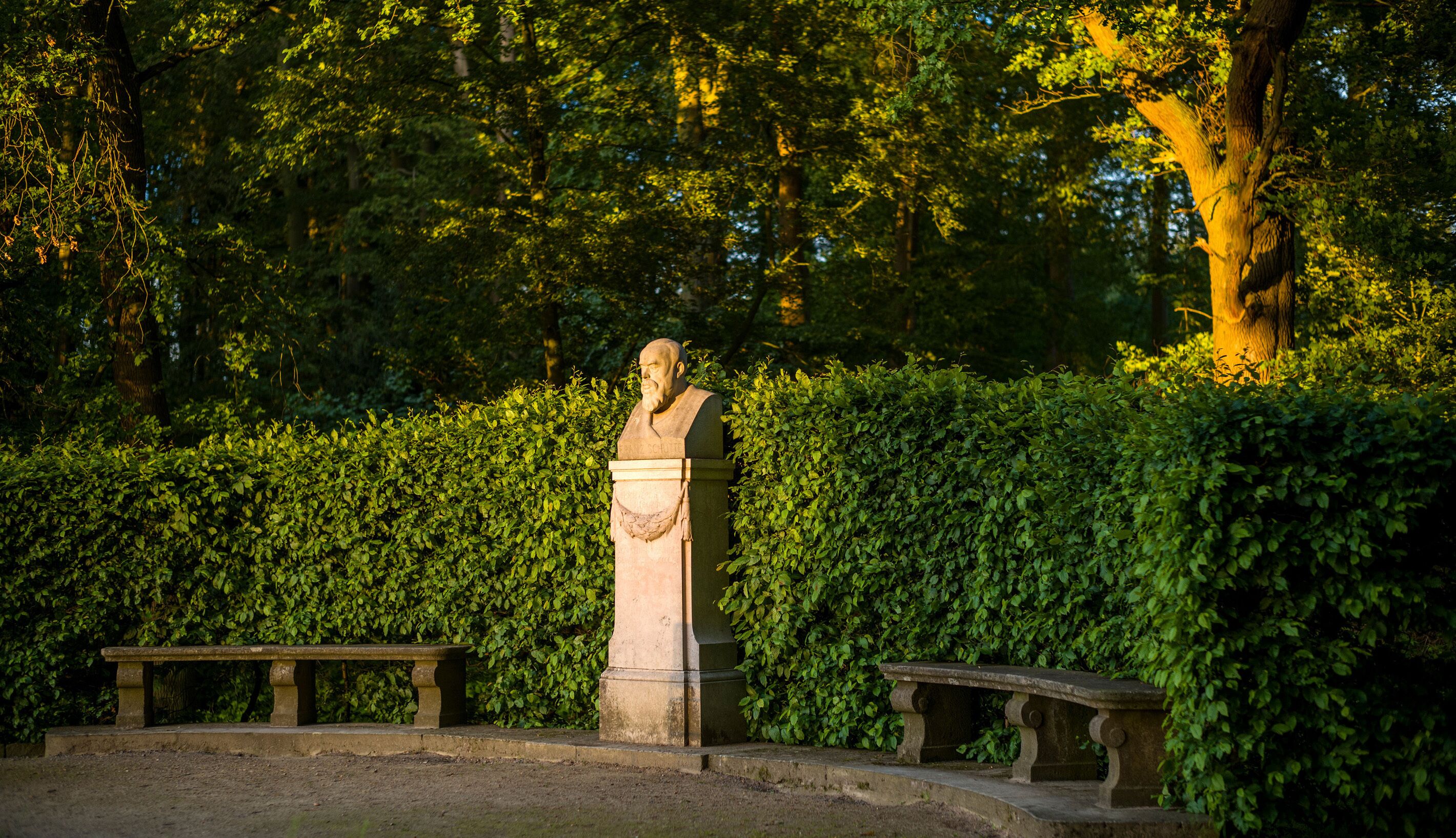 Uma estátua em um parque, com bancos e vegetação densa.