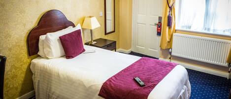 Quarto de hotel com cama bem arrumada, mesa de cabeceira com abajur, espelho, porta e janela com cortinas.
