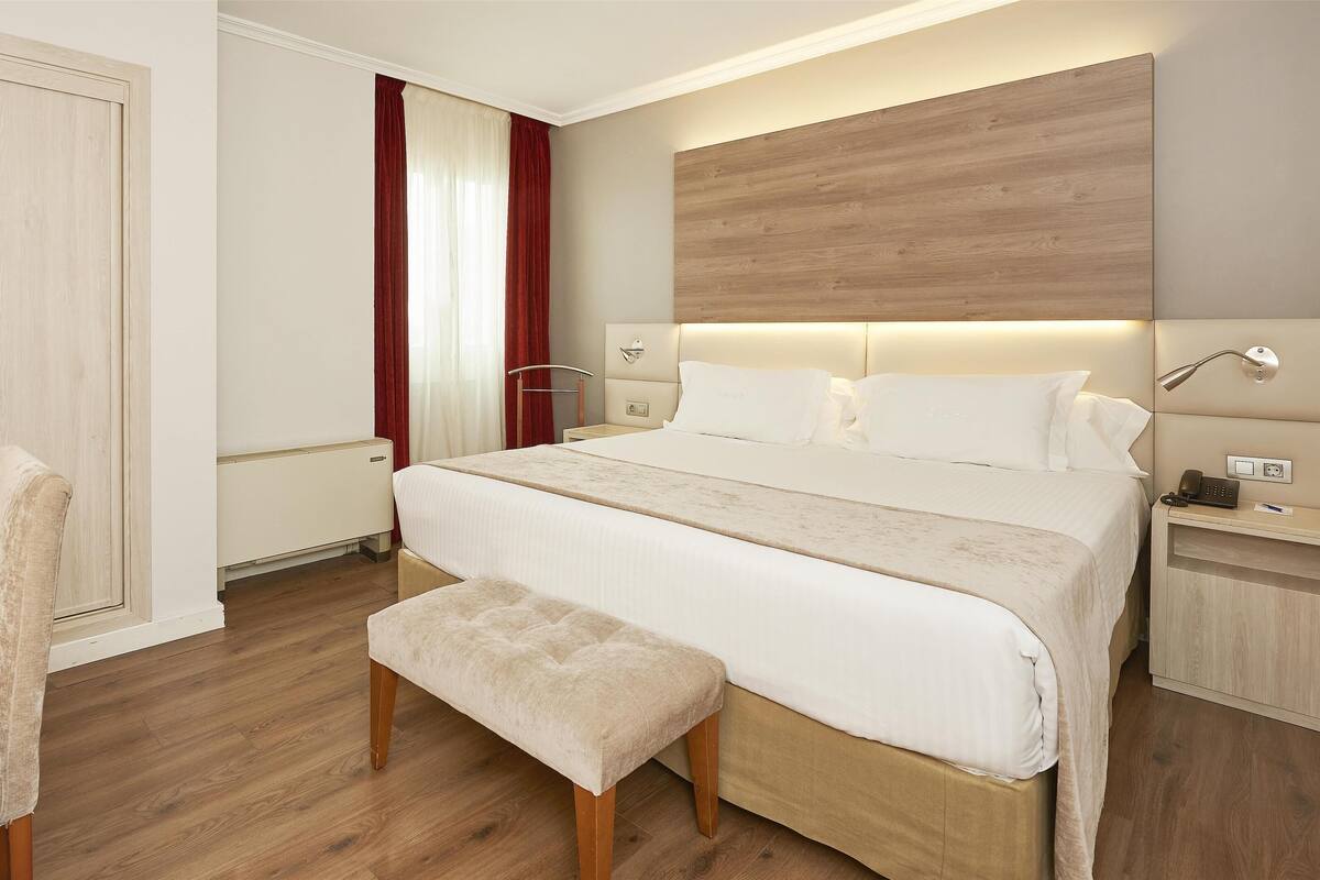 Quarto de hotel com uma cama grande, mesas de cabeceira, escrivaninha com cadeira, guarda-roupa e banheiro.
